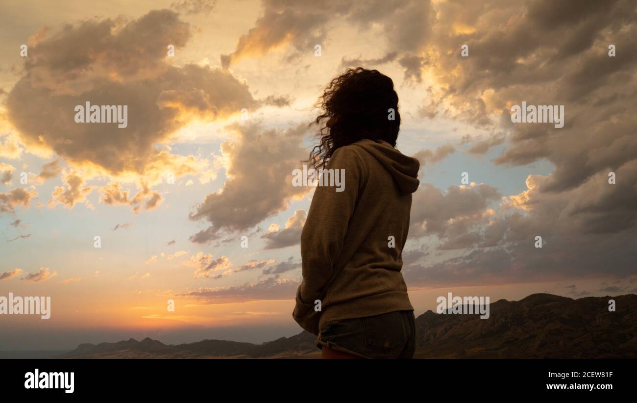 Back view of a female standing under the cloudy sunset sky Stock Photo ...