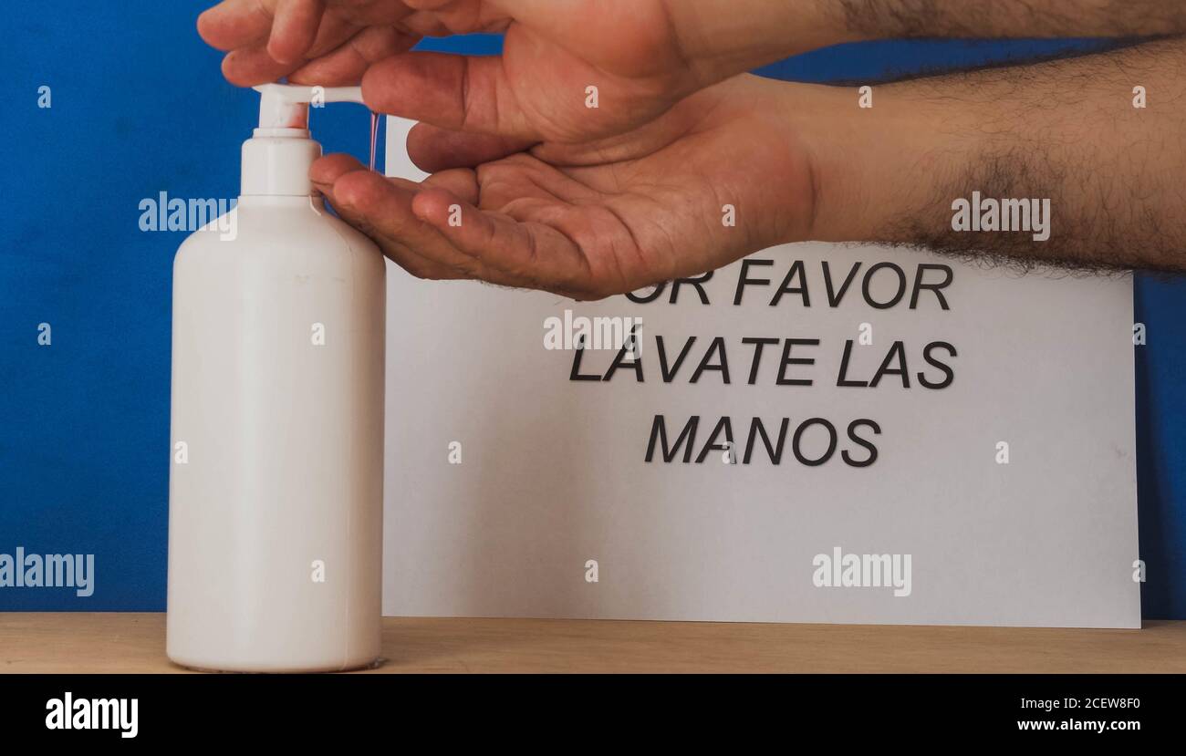 Hands of a person using a hand sanitizer with the message "Please wash ...