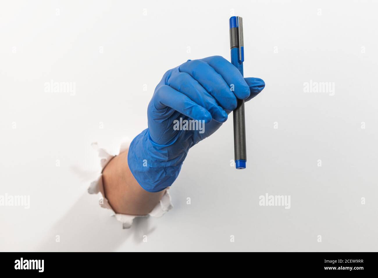 Hand in a latex glow giving a pen through torn white wall Stock Photo ...