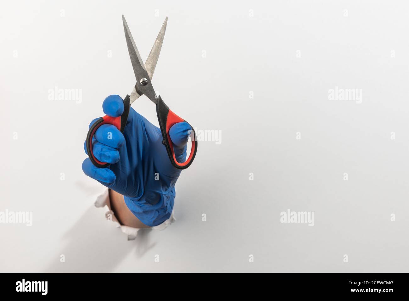 Hand in a latex glove holding scissors through torn white wall Stock ...