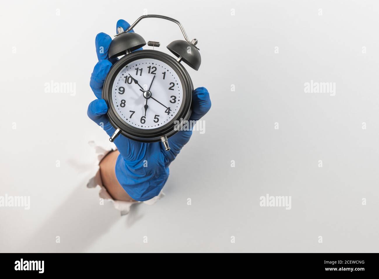 Hand in a latex glove holding a vintage alarm clock through torn white ...
