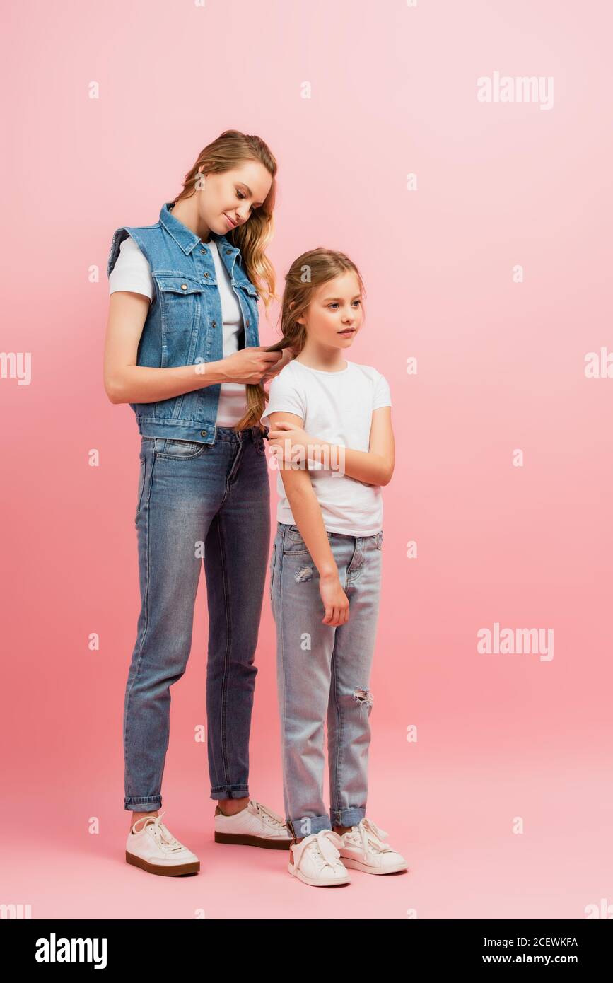 full length view of woman in denim clothes braiding hair of daughter ...