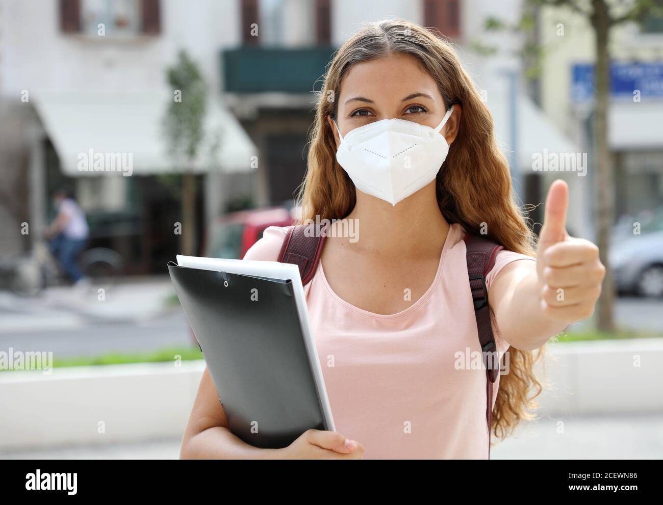 Optimistic student girl back to school with protective mask shows thumb ...