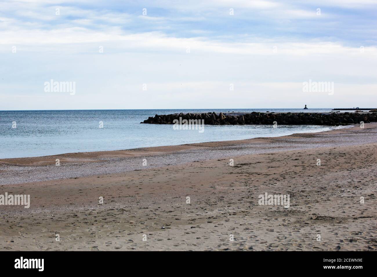 Closeup shot of a sandy beach with the ocean and a stone dock on the ...