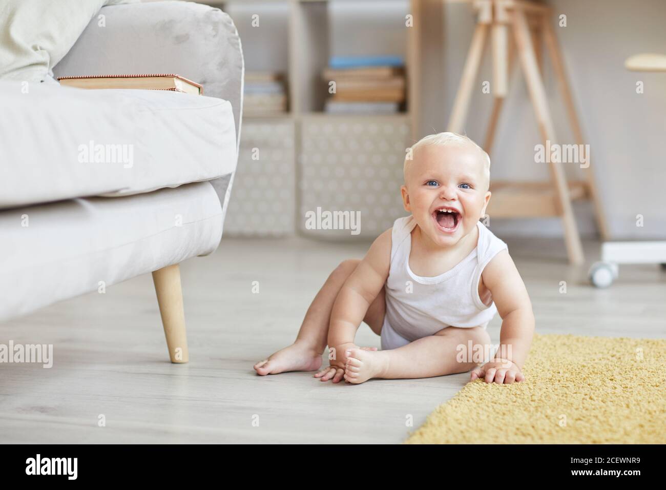 Horizontal shot of happy playful baby sitting on floor in living room ...