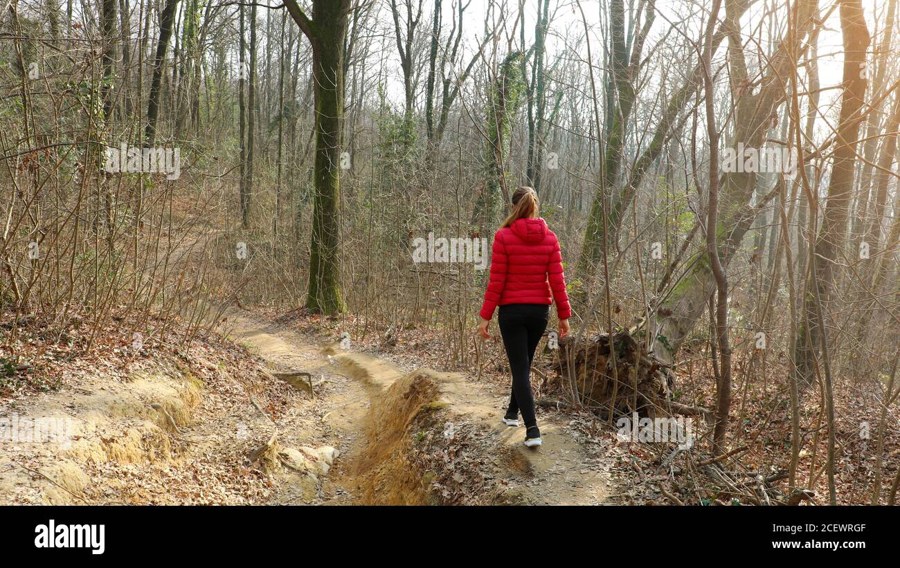 Young woman walking away alone on a forest path wearing a red down ...