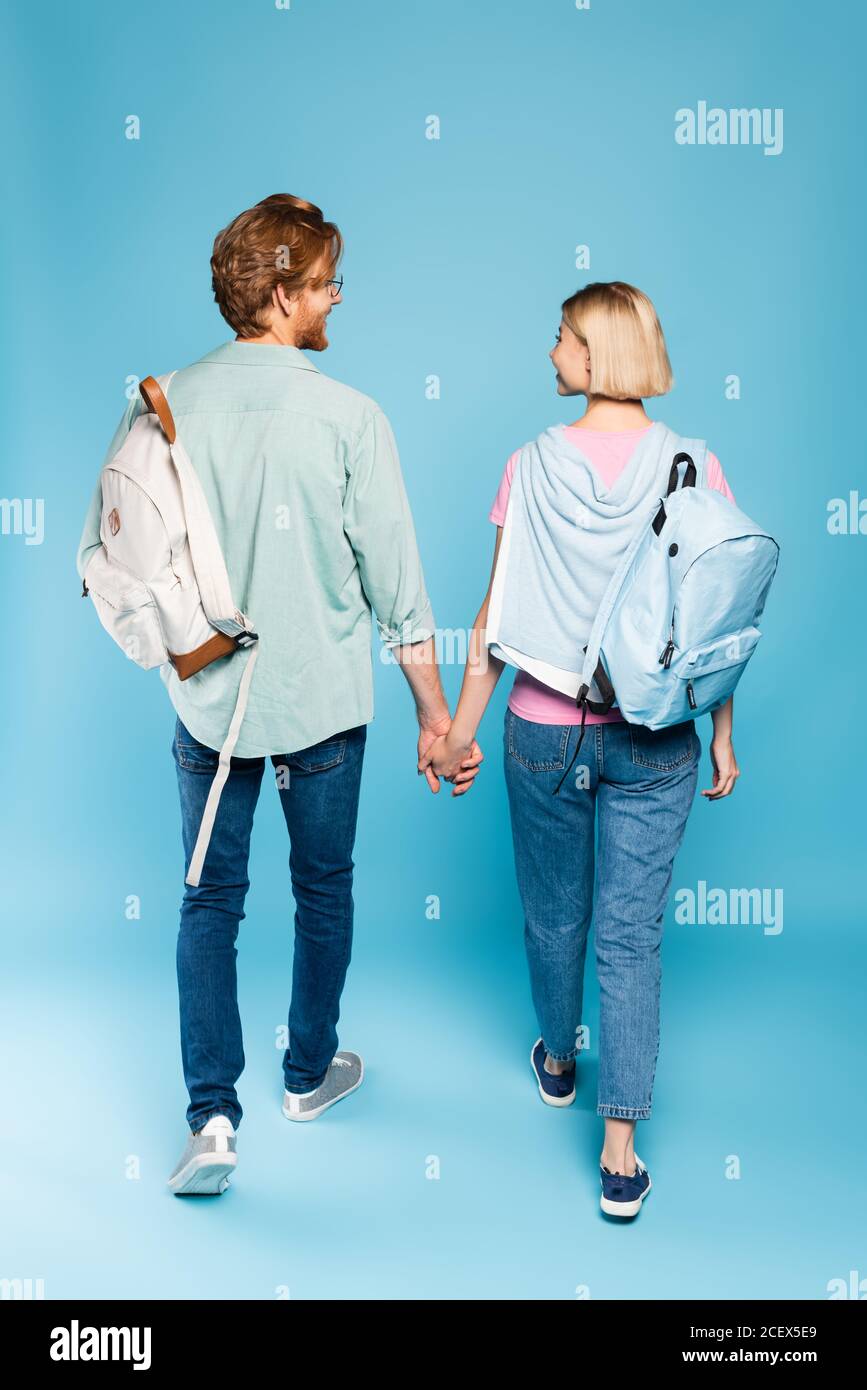 back view of young students with backpacks holding hands while walking ...