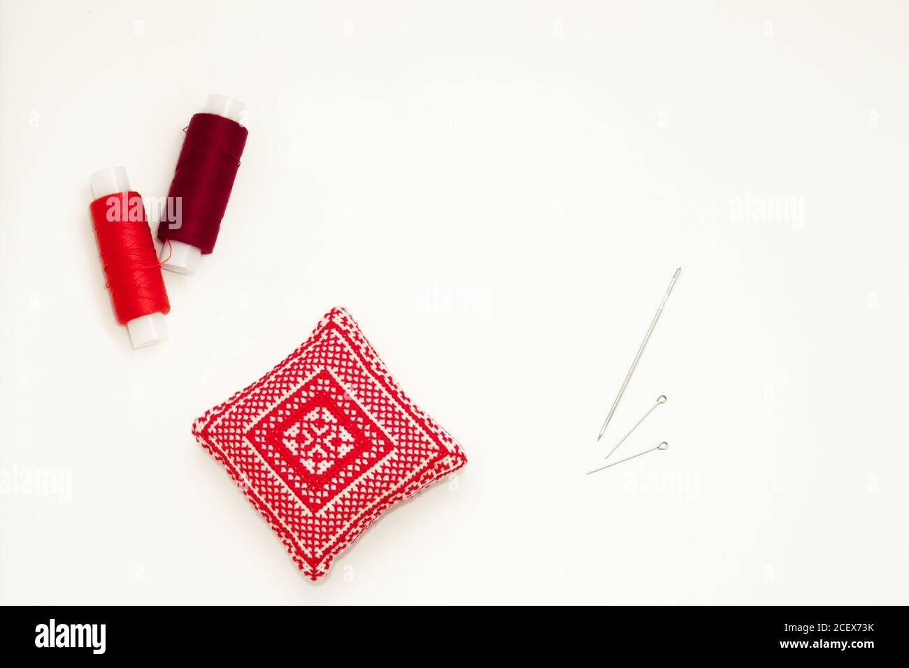 Flat lay with handmade red embroidered needle pad, thread spools, pins ...