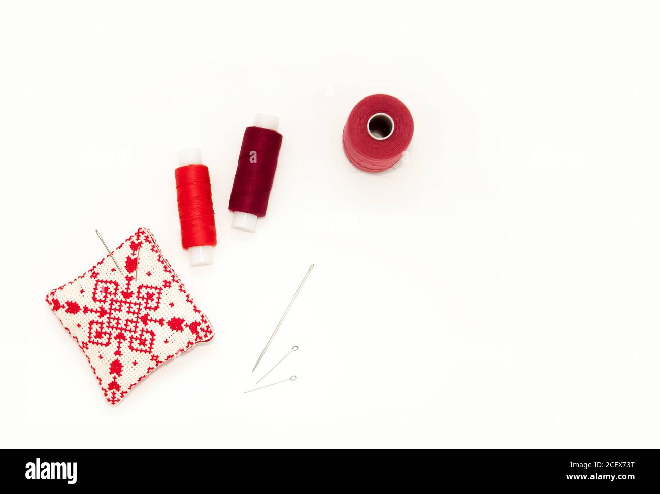Flat lay with handmade red embroidered needle pad, thread spools, pins ...