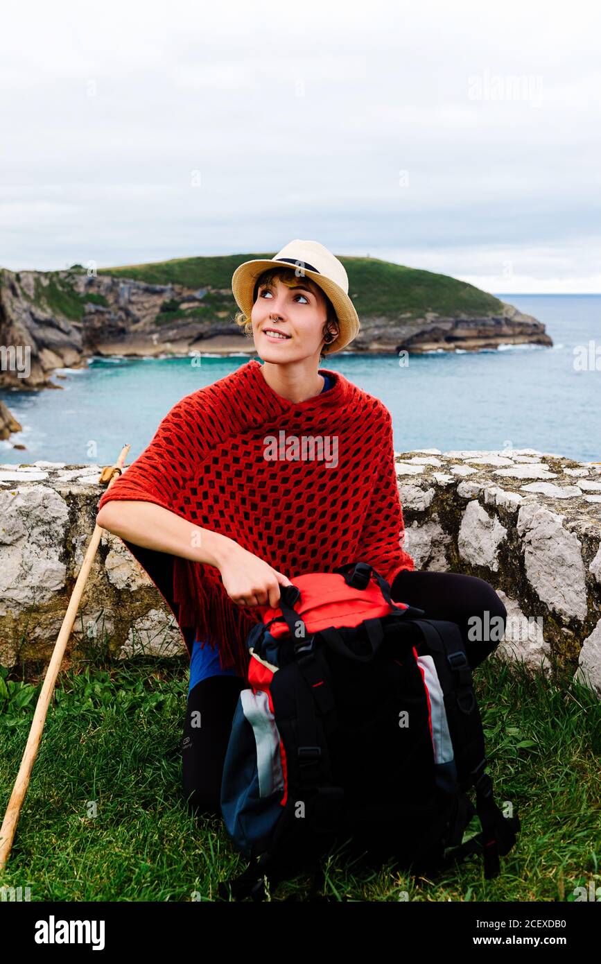 Full body of happy young female backpacker in stylish clothes sitting ...