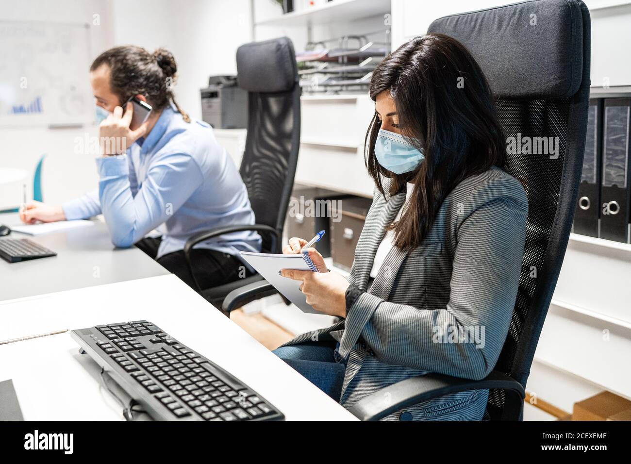 Serious young female employee in formal clothes and protective mask ...