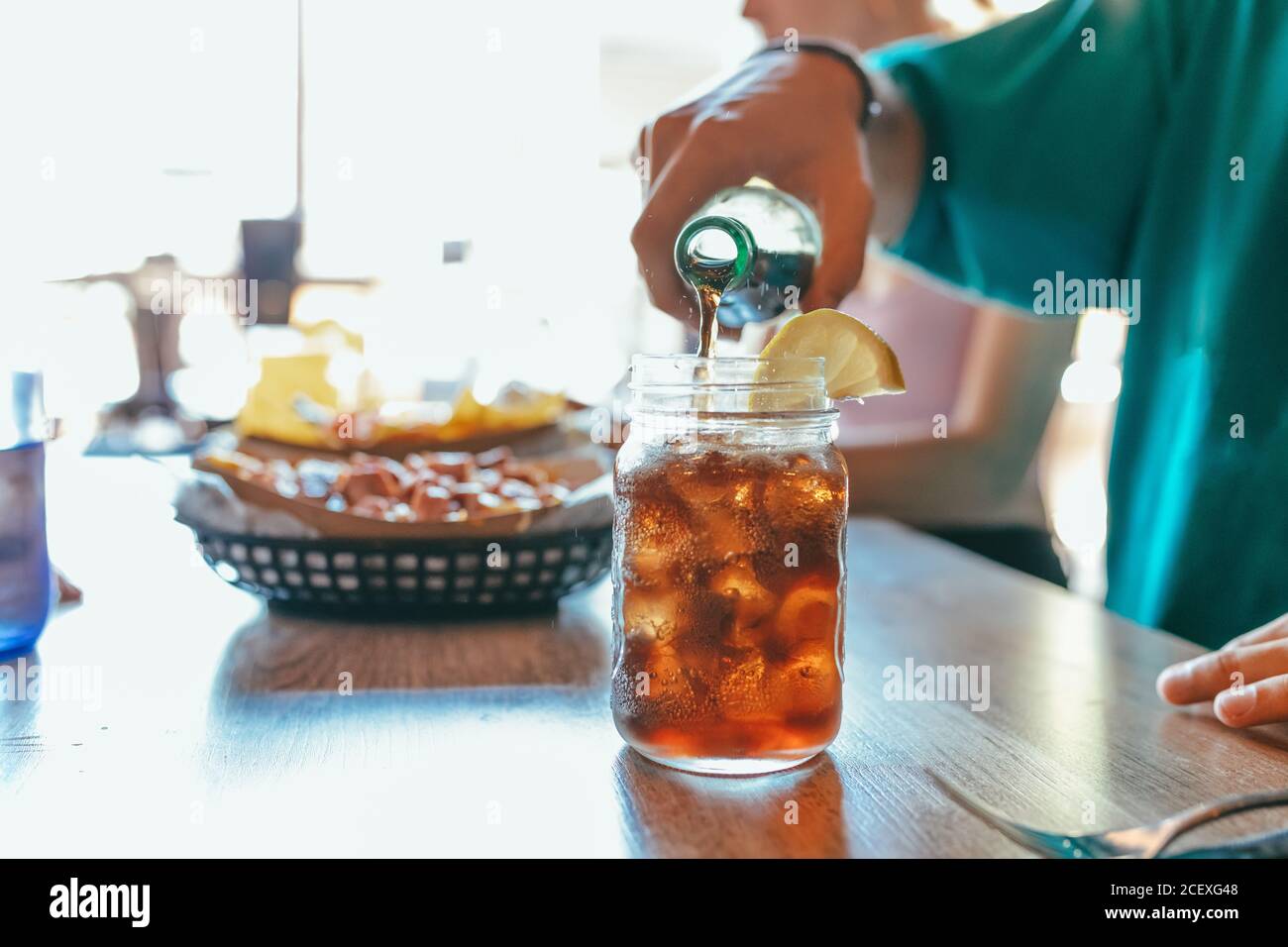 Crop unrecognizable male pouring cold drink from bottle into glass cup ...