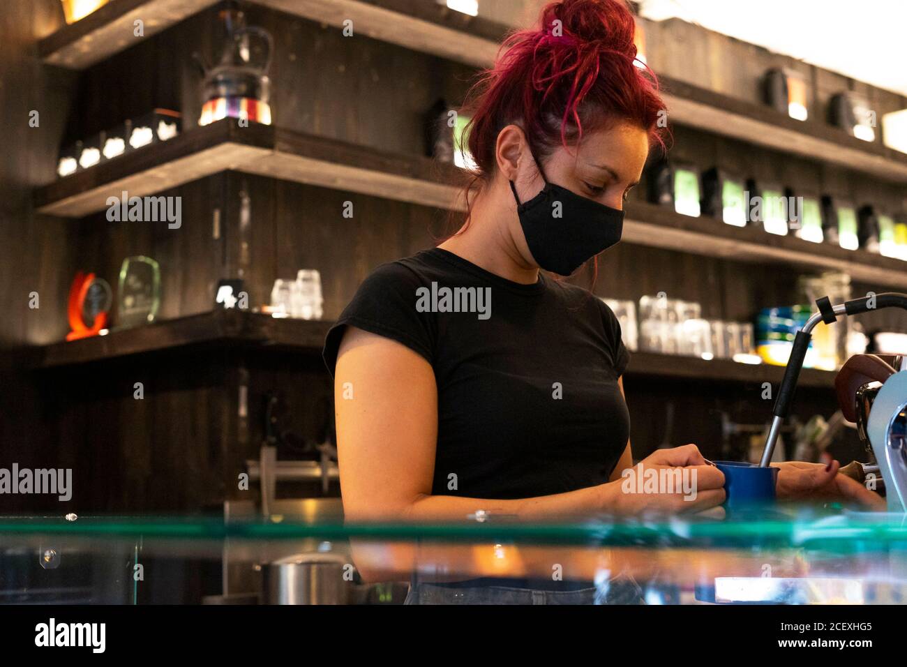 Side view of female bartender in face mask standing at counter in ...