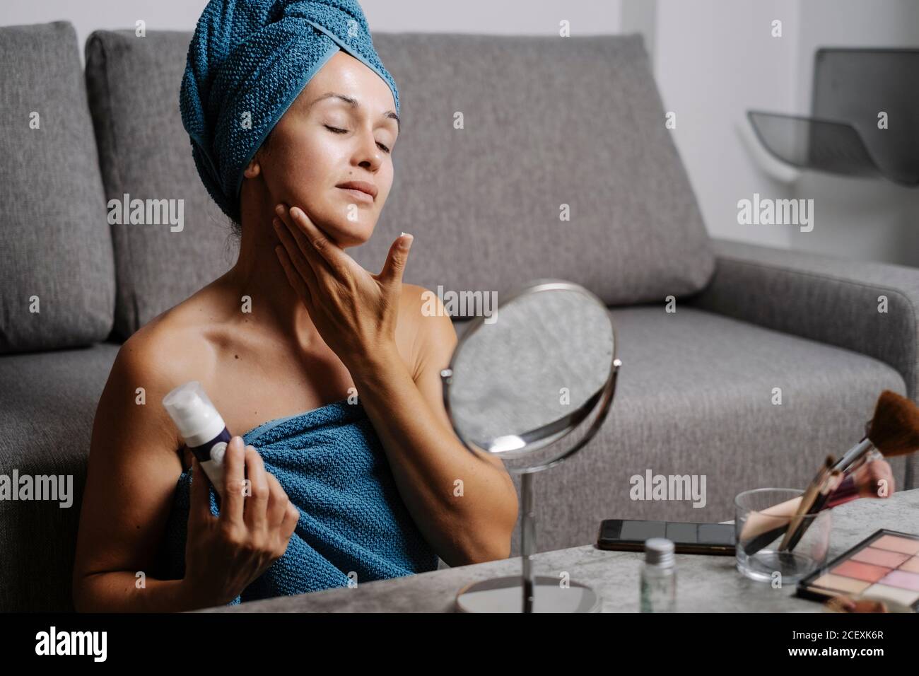 Charming young female with bare shoulders and towel on head smearing ...