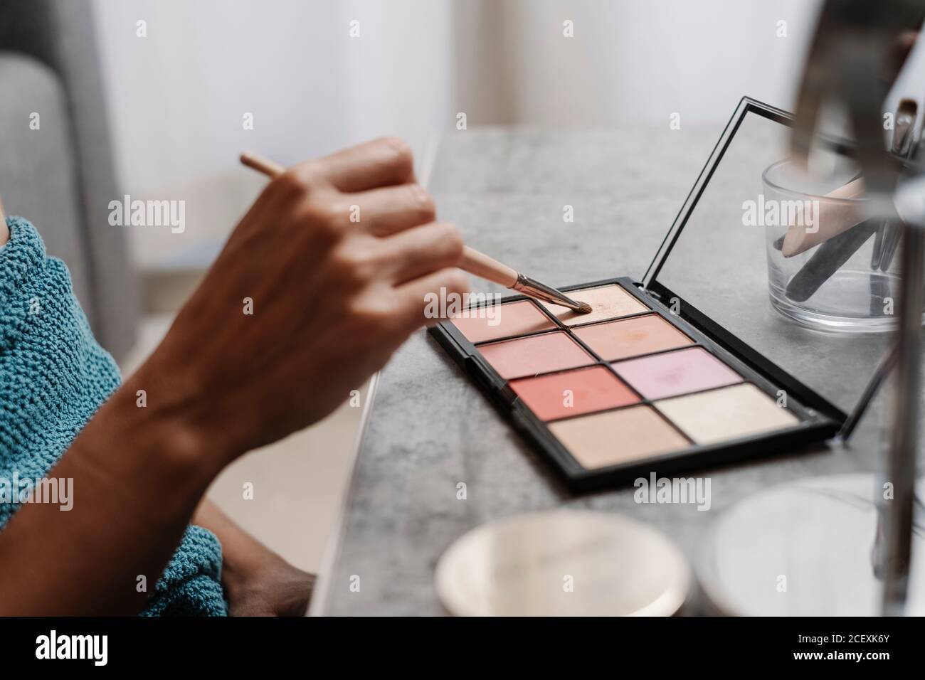 Side view of crop anonymous female taking eye shadow from palette with ...