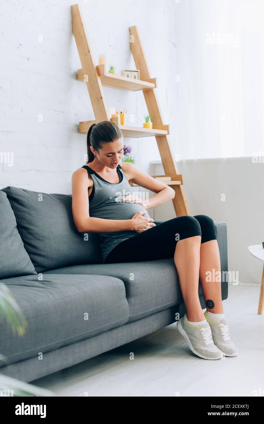 Selective focus of pregnant sportswoman feeling pain and touching belly ...