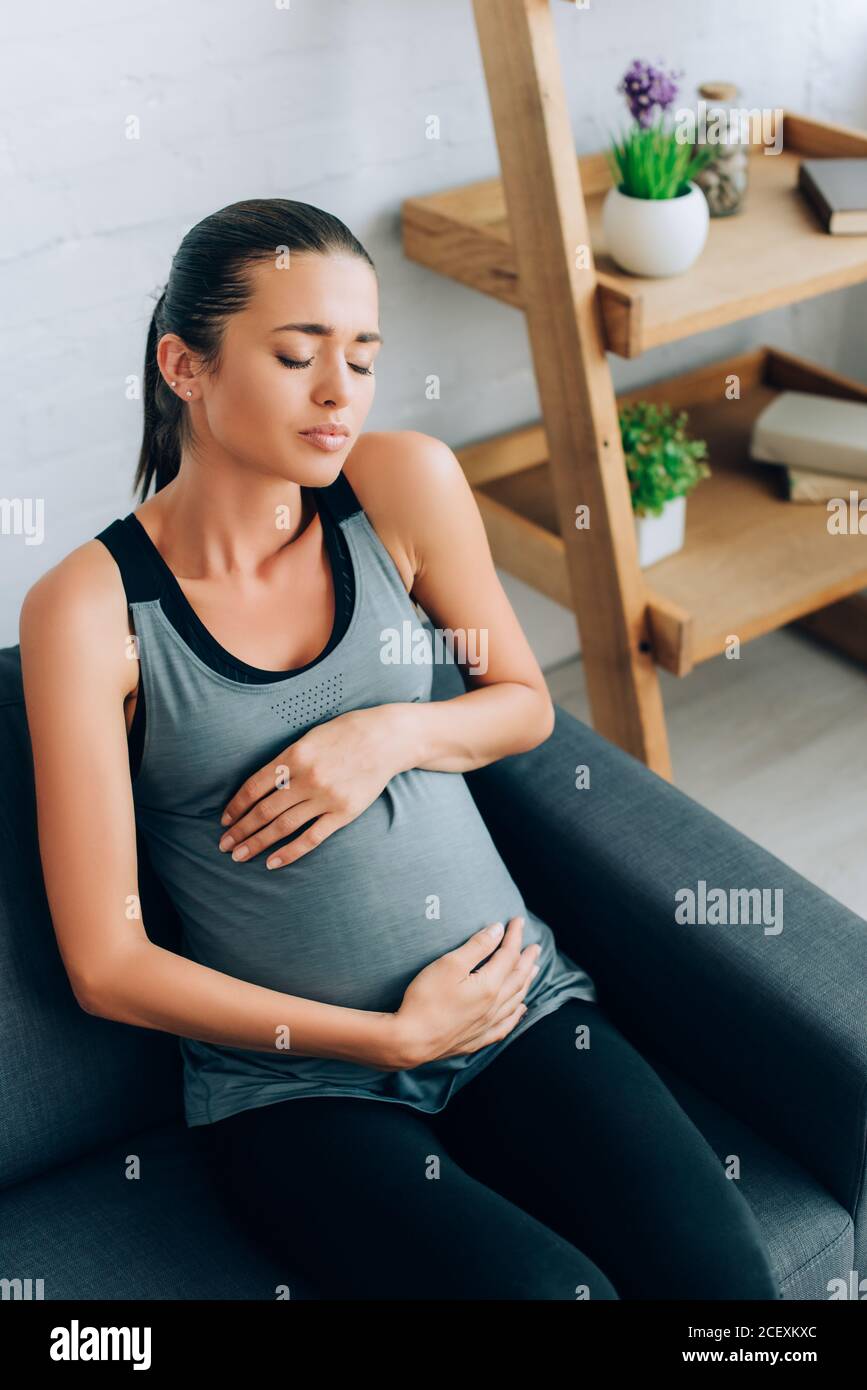 Pregnant sportswoman feeling pain and embracing belly on couch Stock ...