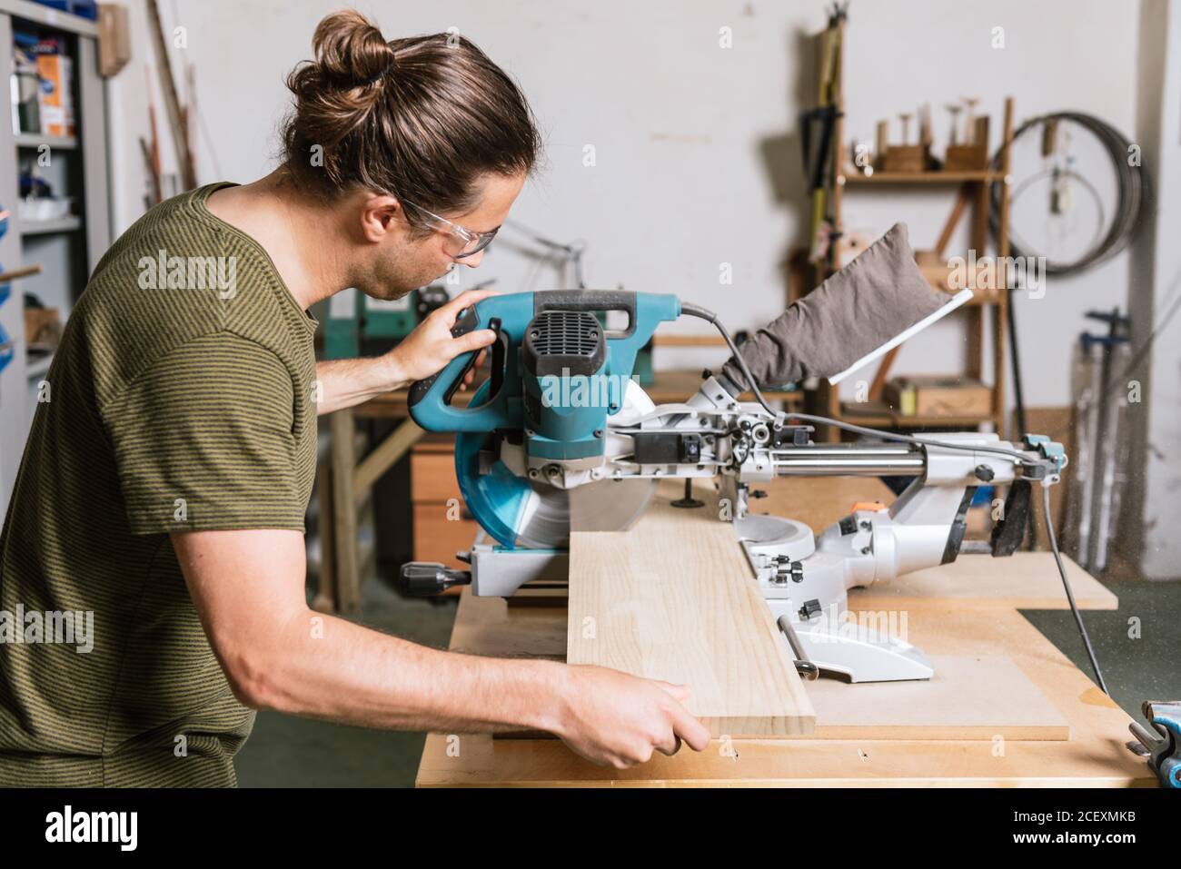 Side view of male carpenter in protective goggles cutting wooden plank ...