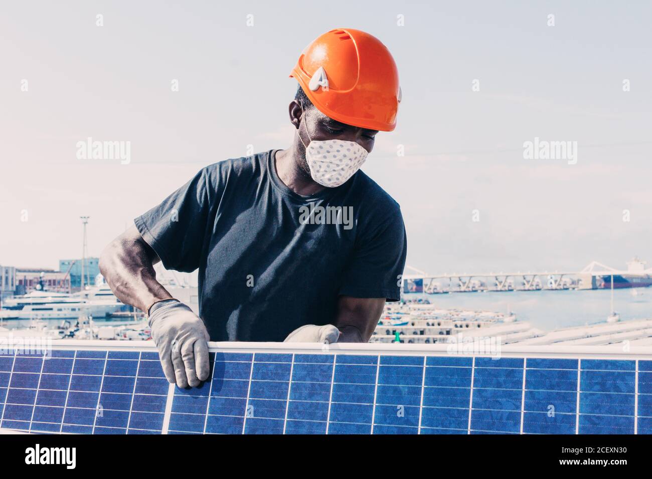 Black workman in helmet and protective mask installing solar battery in ...