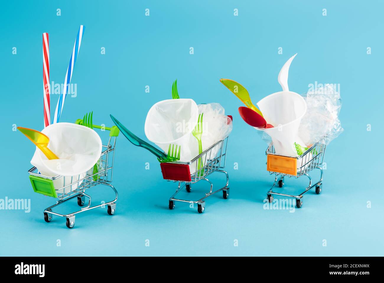 disposable plastic objects in small shopping carts on blue background ...