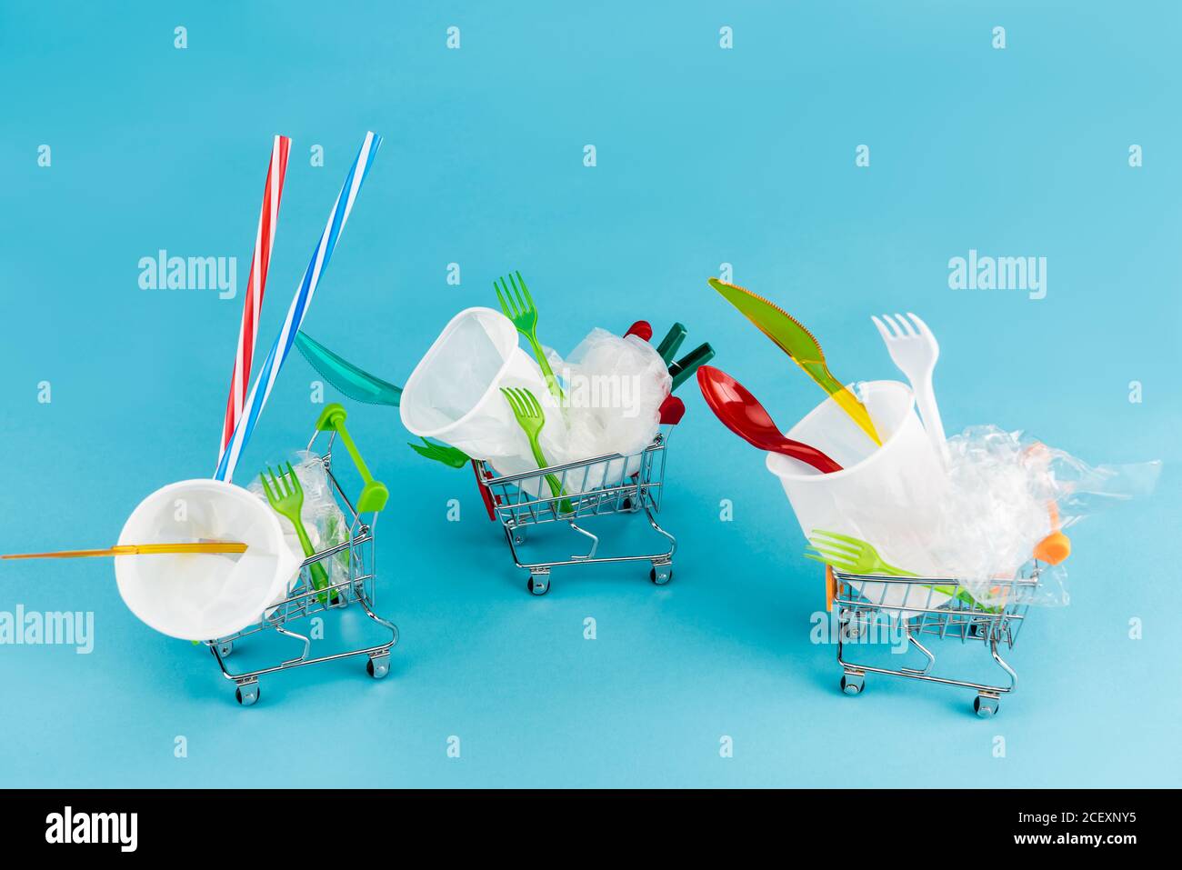 disposable plastic objects in small shopping carts on blue background ...