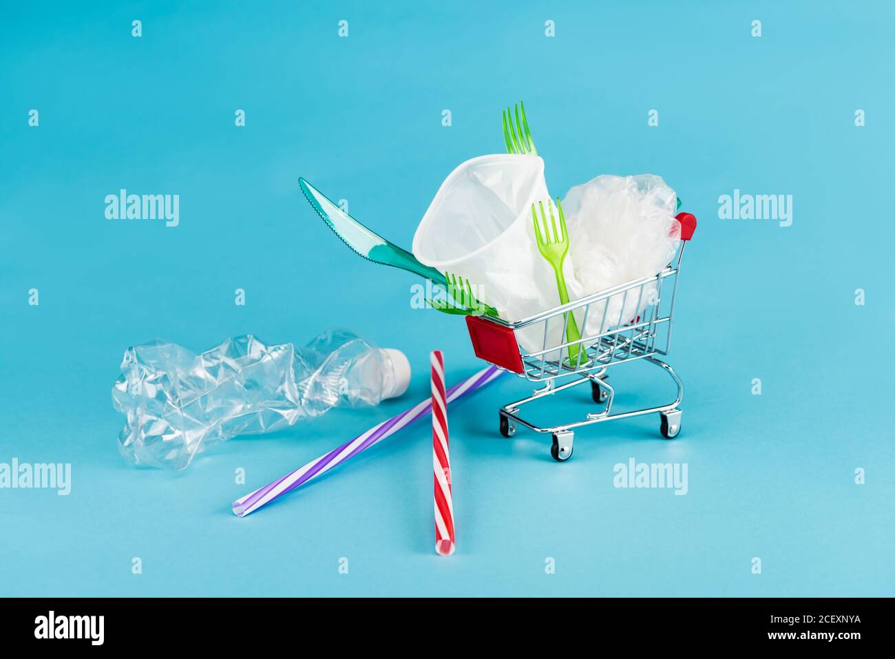 disposable plastic objects in small shopping cart on blue background ...