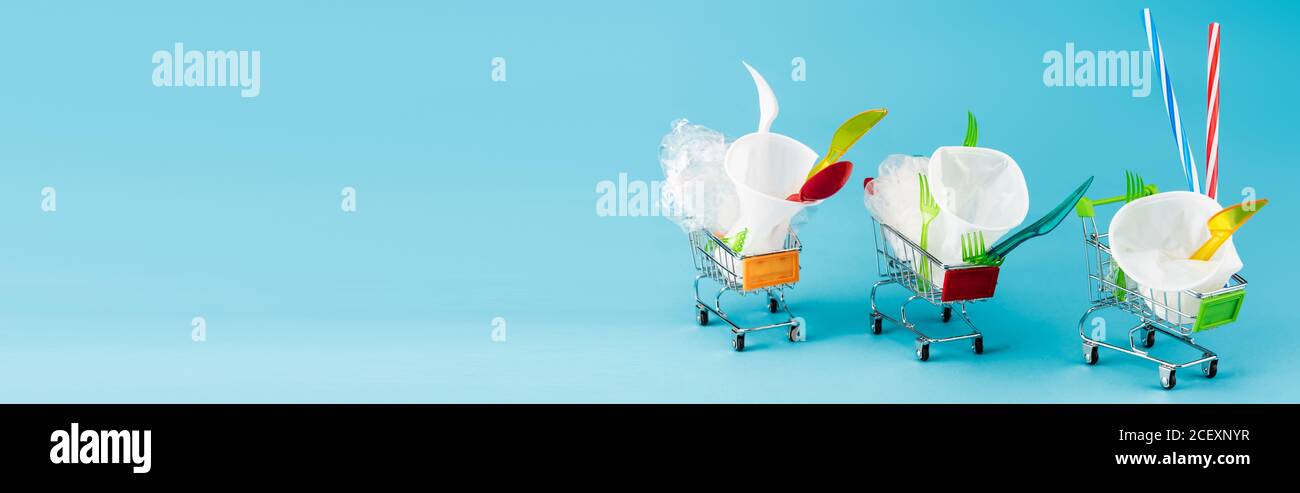 disposable plastic objects in small shopping carts on blue background ...