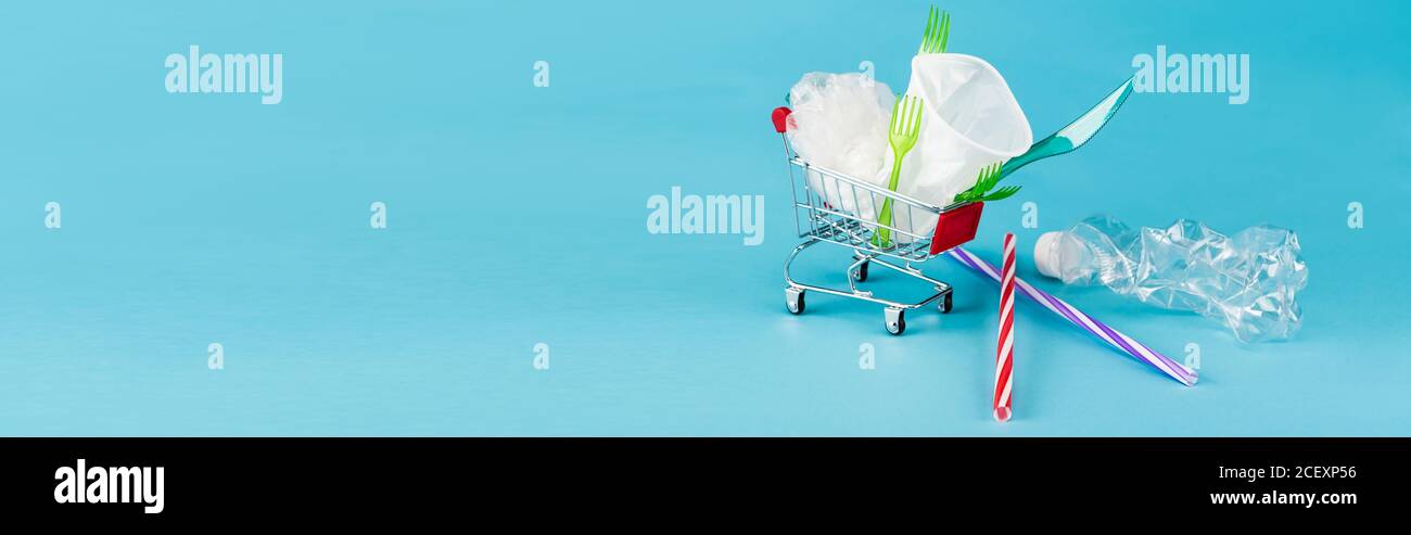 disposable plastic objects in small shopping cart on blue background ...