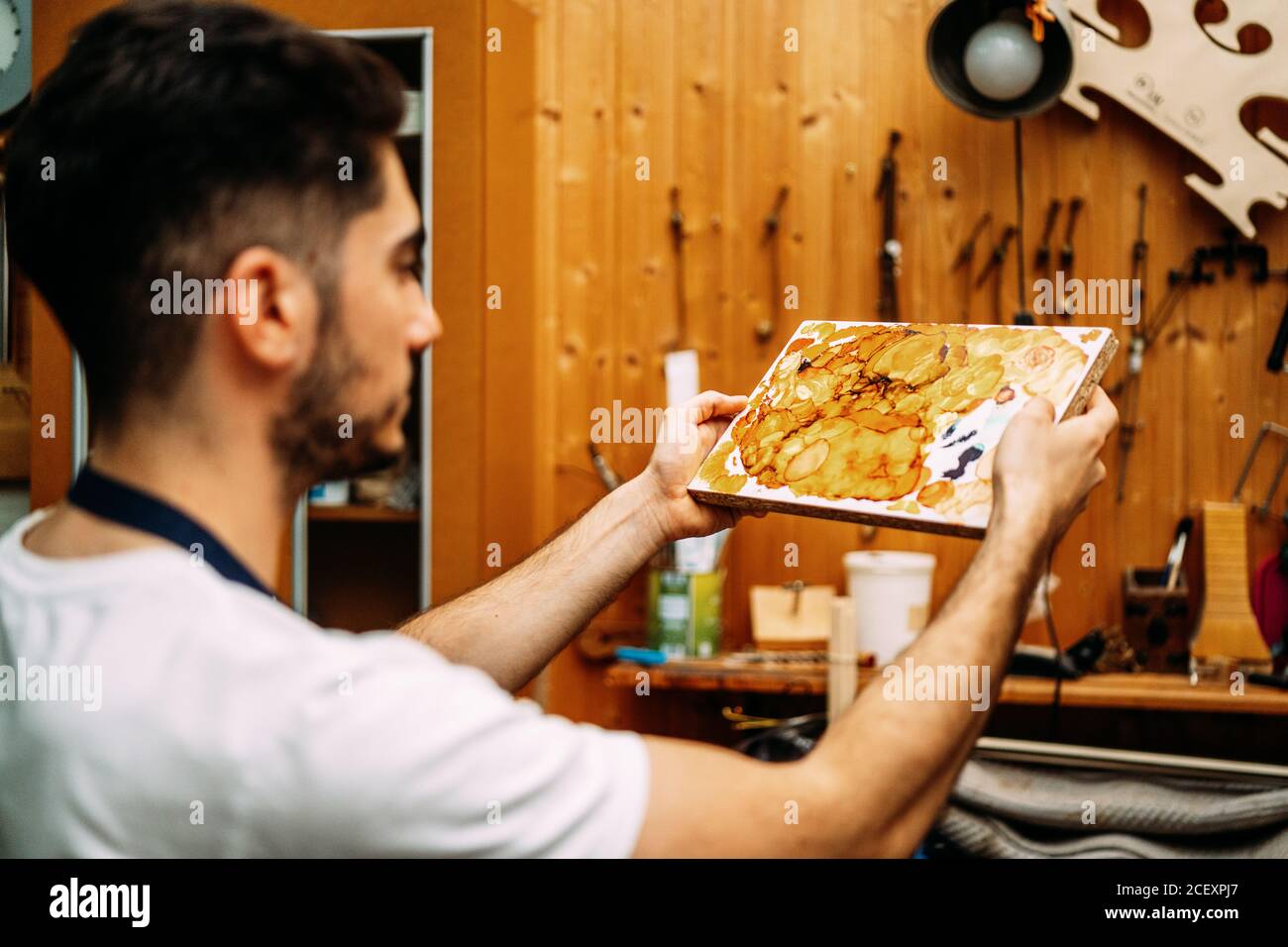 Side view of young male artisan luthier standing at counter and holding ...