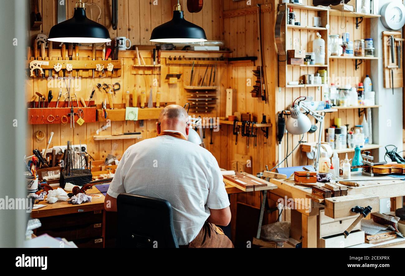 Back view of unrecognizable male luthier master sitting on chair and ...