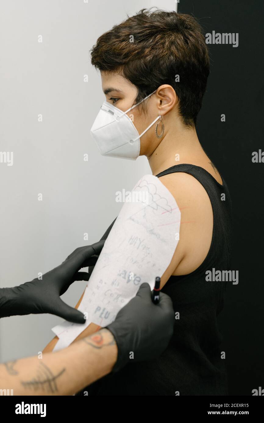 anonymous crop tattoo master applying stencil on arm of customer while ...
