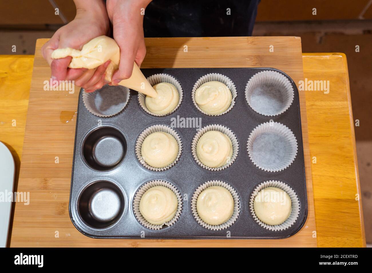 Top view of anonymous cook with pastry bag making muffins and pouring ...