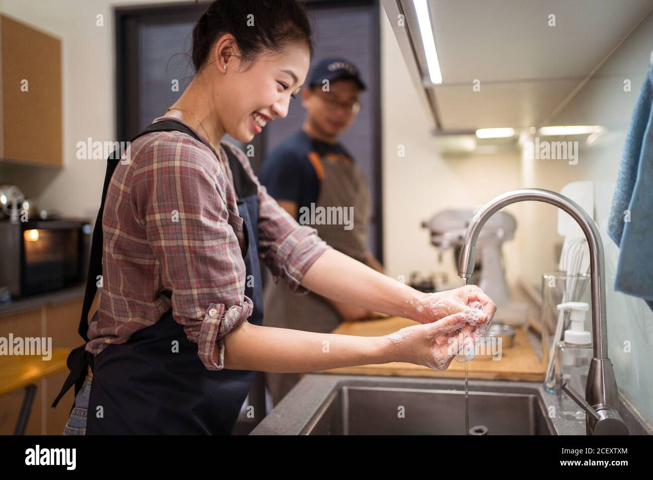 Side view of cheerful Asian Woman washing hands in sink while having ...