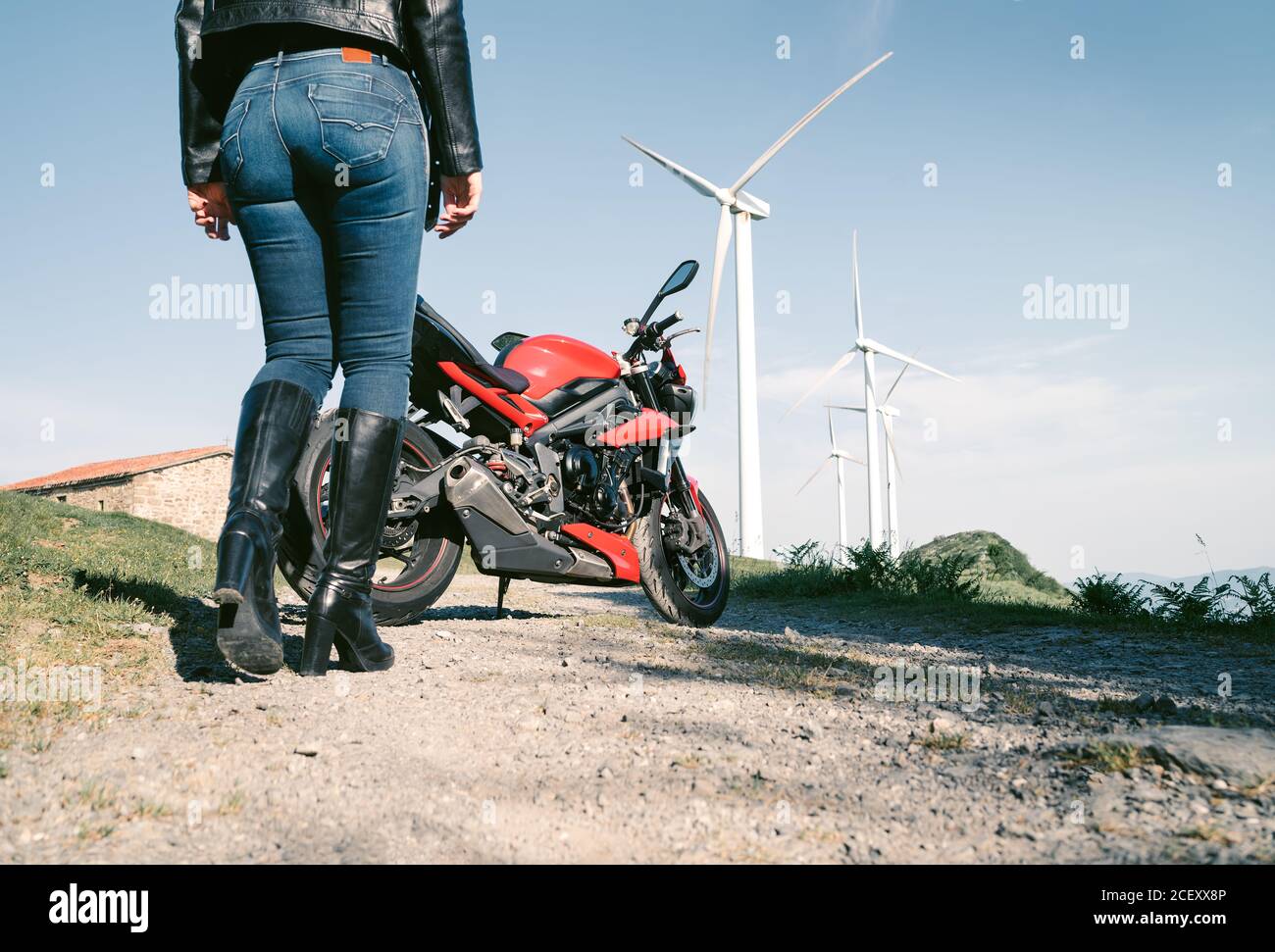 Low angle back view of crop female motorcyclist walking towards modern ...