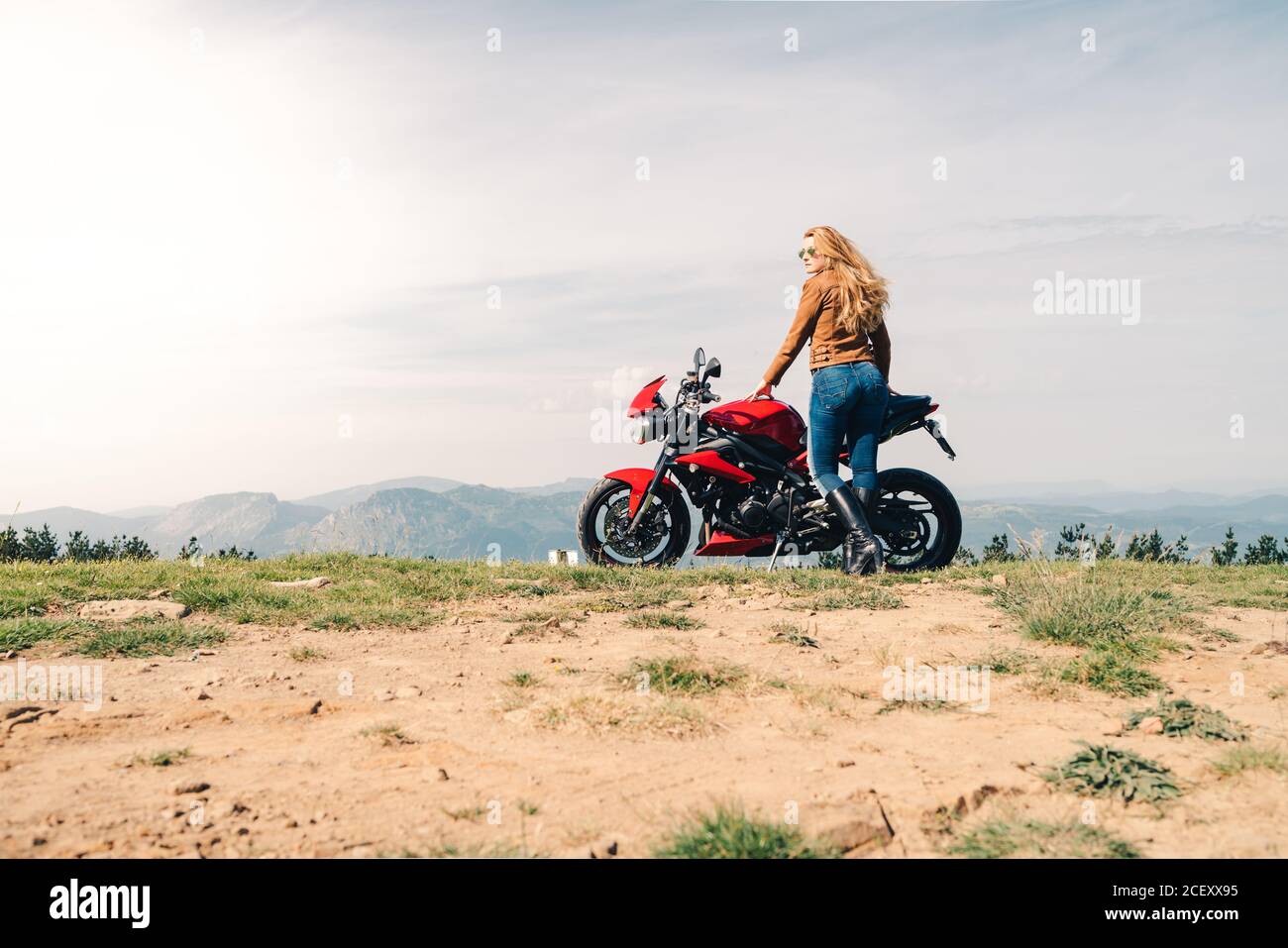 Back view low angle of brutal female biker standing near motorbike on ...