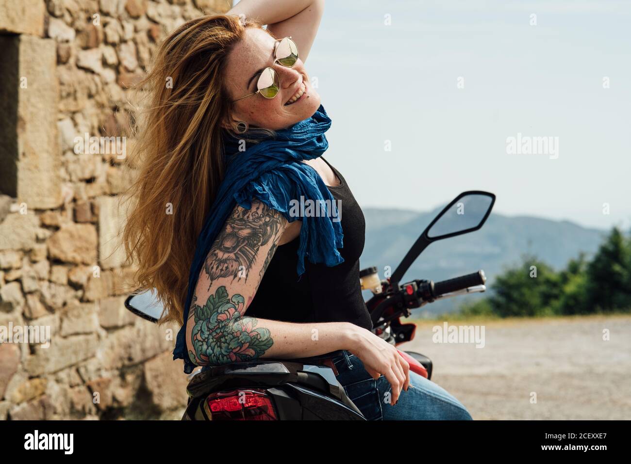 Side view of cheerful female motorcyclist leaning on sport motorbike ...