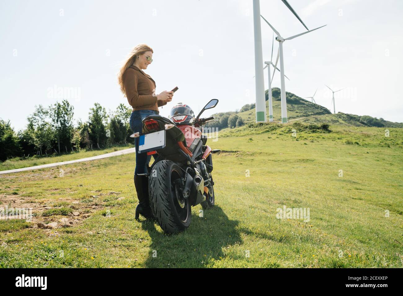 Low angle of delighted female motorcyclist standing near contemporary ...