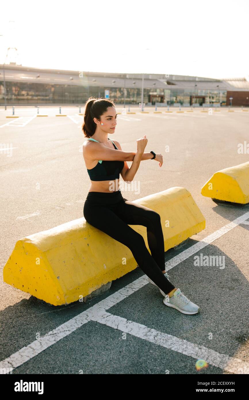 Full body of young slim female runner in black sportswear sitting on ...