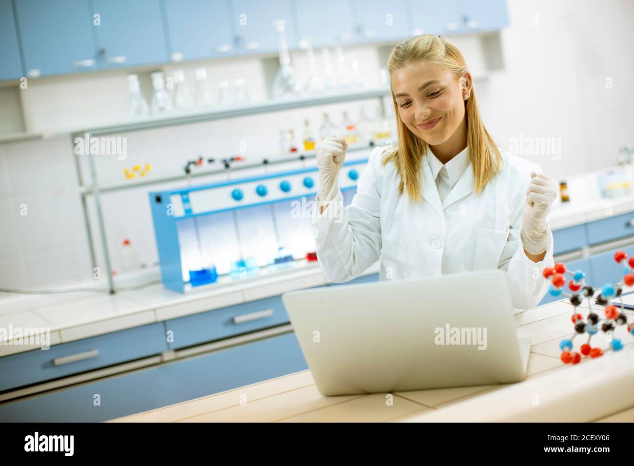 Cute happy female researcher in white lab coat using laptop while ...