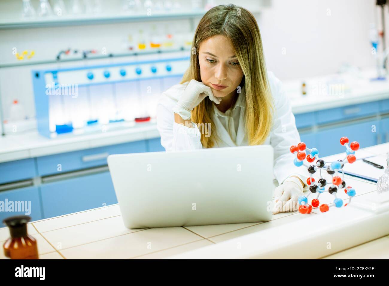 Cute female researcher in white lab coat using laptop while working in ...