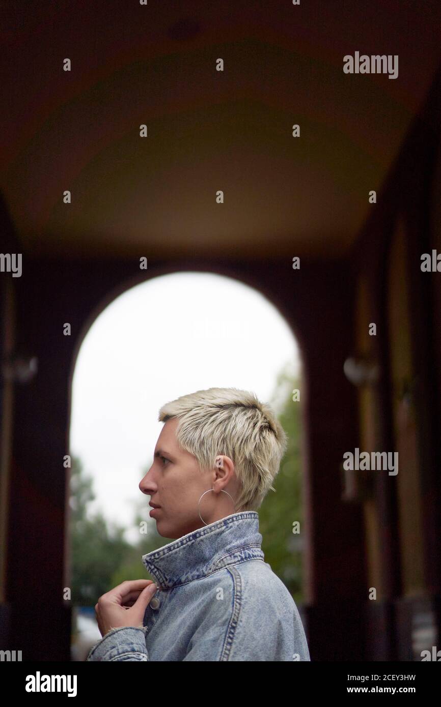 Side view of calm female model wearing denim jacket standing in arched ...