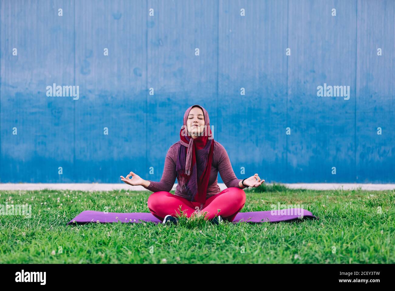 Serene Arab female in sportswear and hijab sitting on mat on lotus pose ...