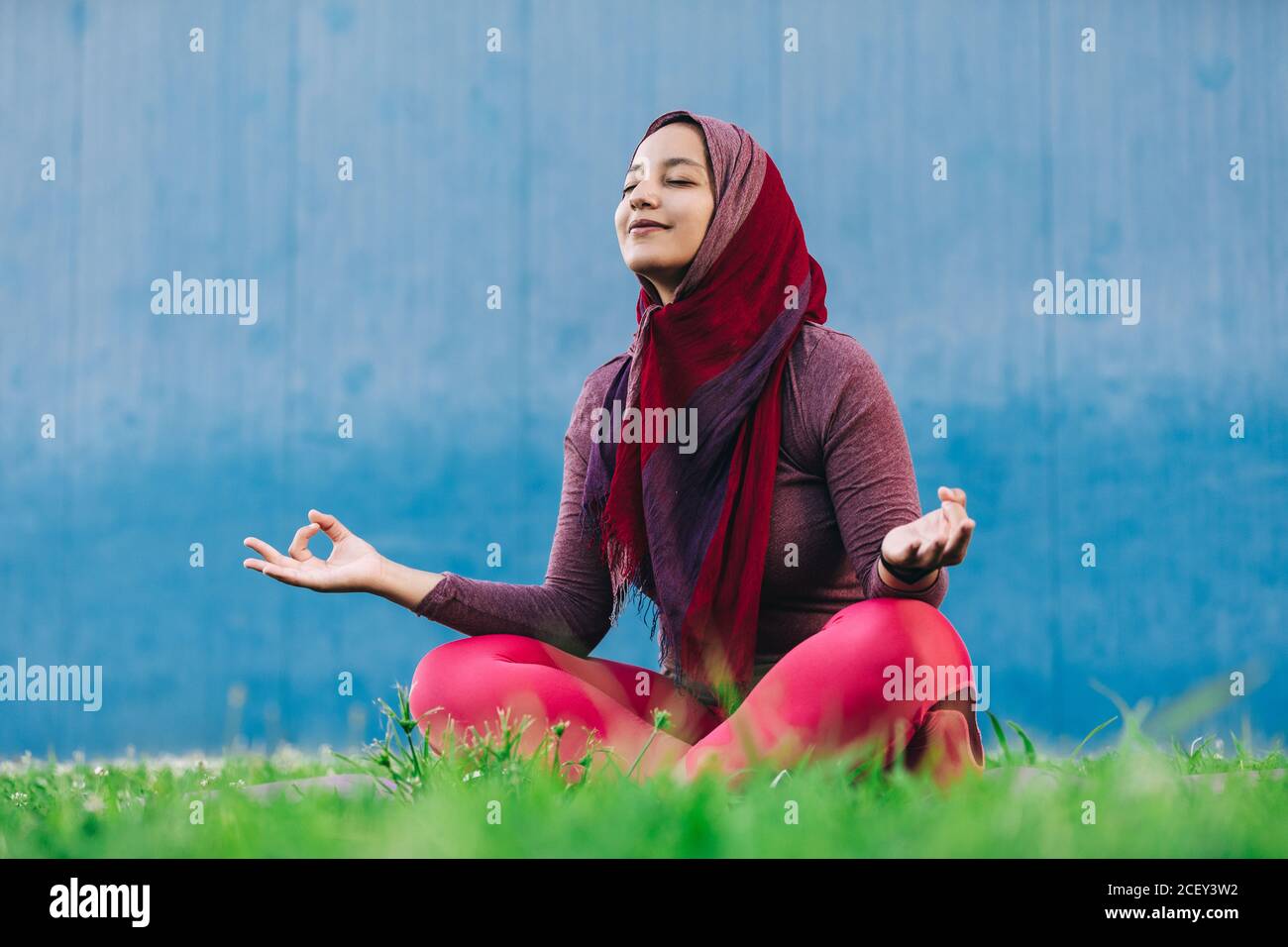 Serene Arab female in sportswear and hijab sitting on mat on lotus pose ...