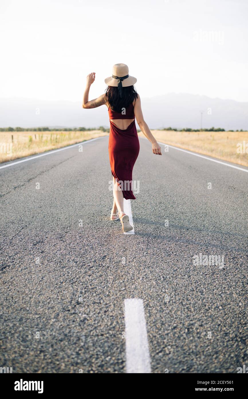 Back view traveler in summer dress and sunhat walking along empty ...