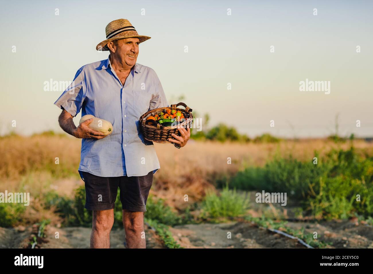Aged male farmer standing barefoot with wicker basket of fresh fruits ...