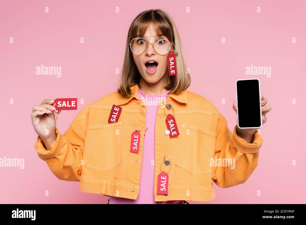 Surprised woman holding price tag with sale word and smartphone with ...