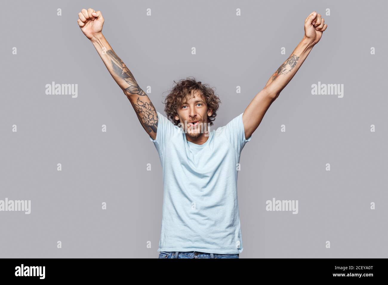 Freestyle. Man with curly hair standing isolated on grey raising hands ...