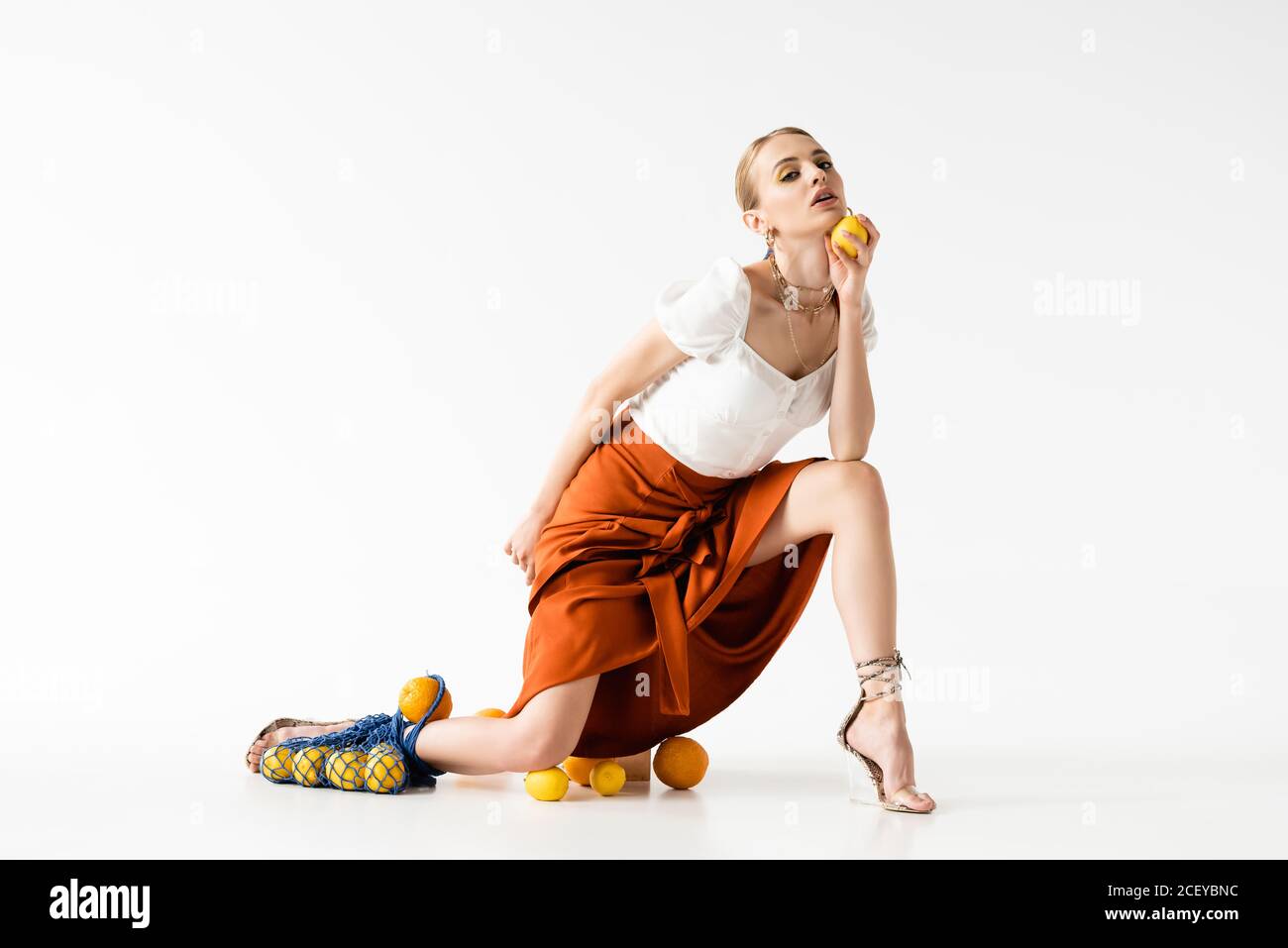 elegant blonde woman posing with string bag near scattered citrus ...