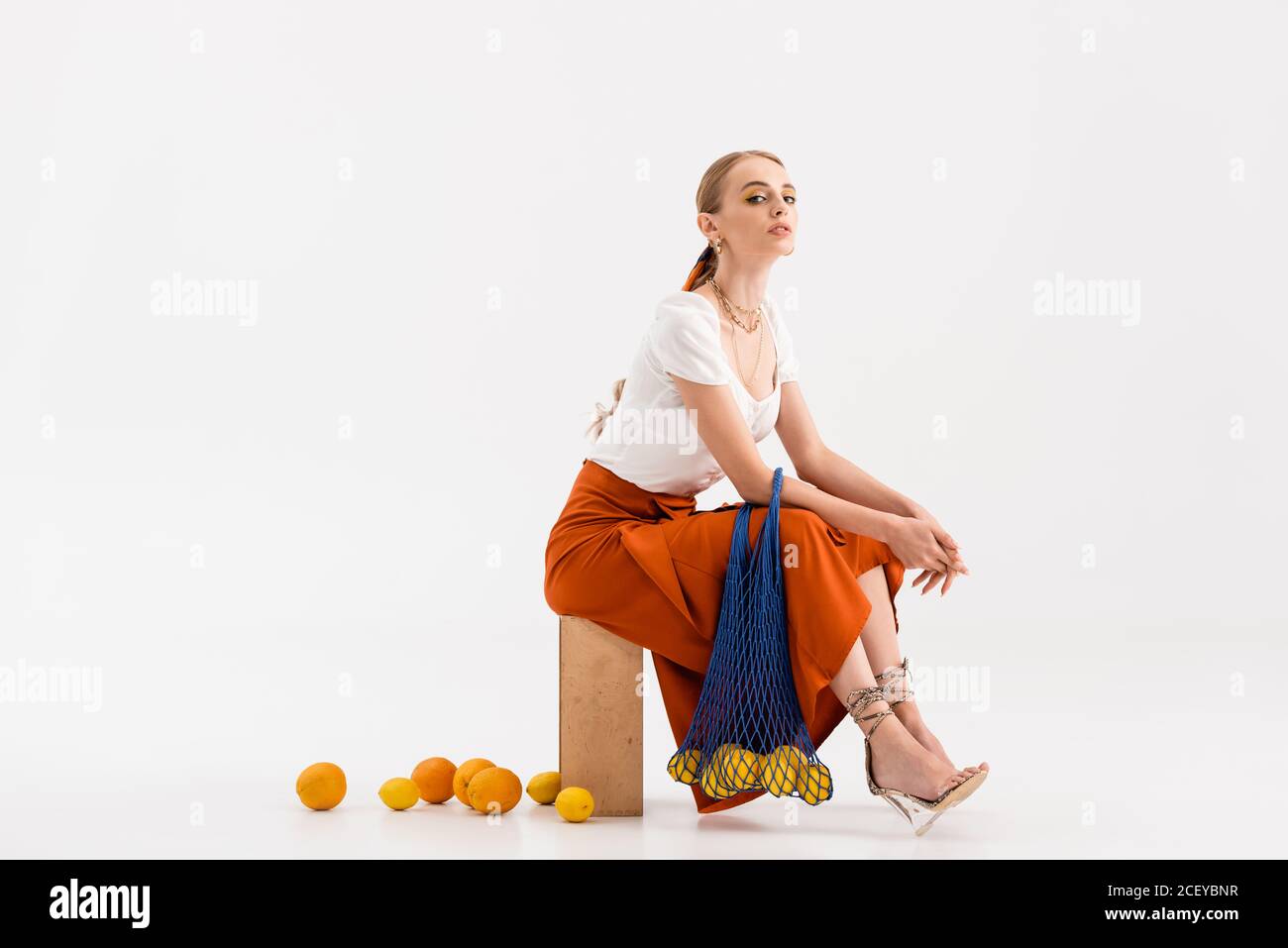 elegant blonde woman posing with string bag near scattered citrus ...