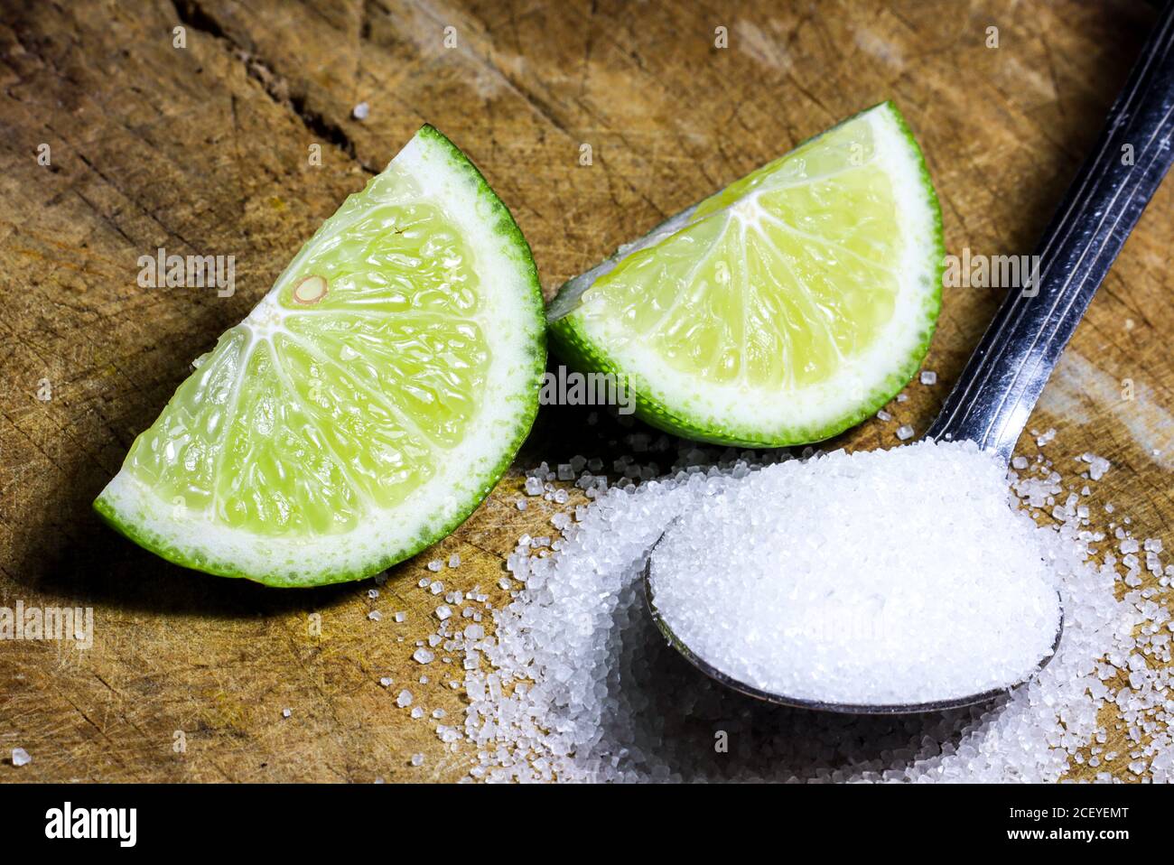 a spoon of granulated sugar and lime slices against a wooden backdrop ...